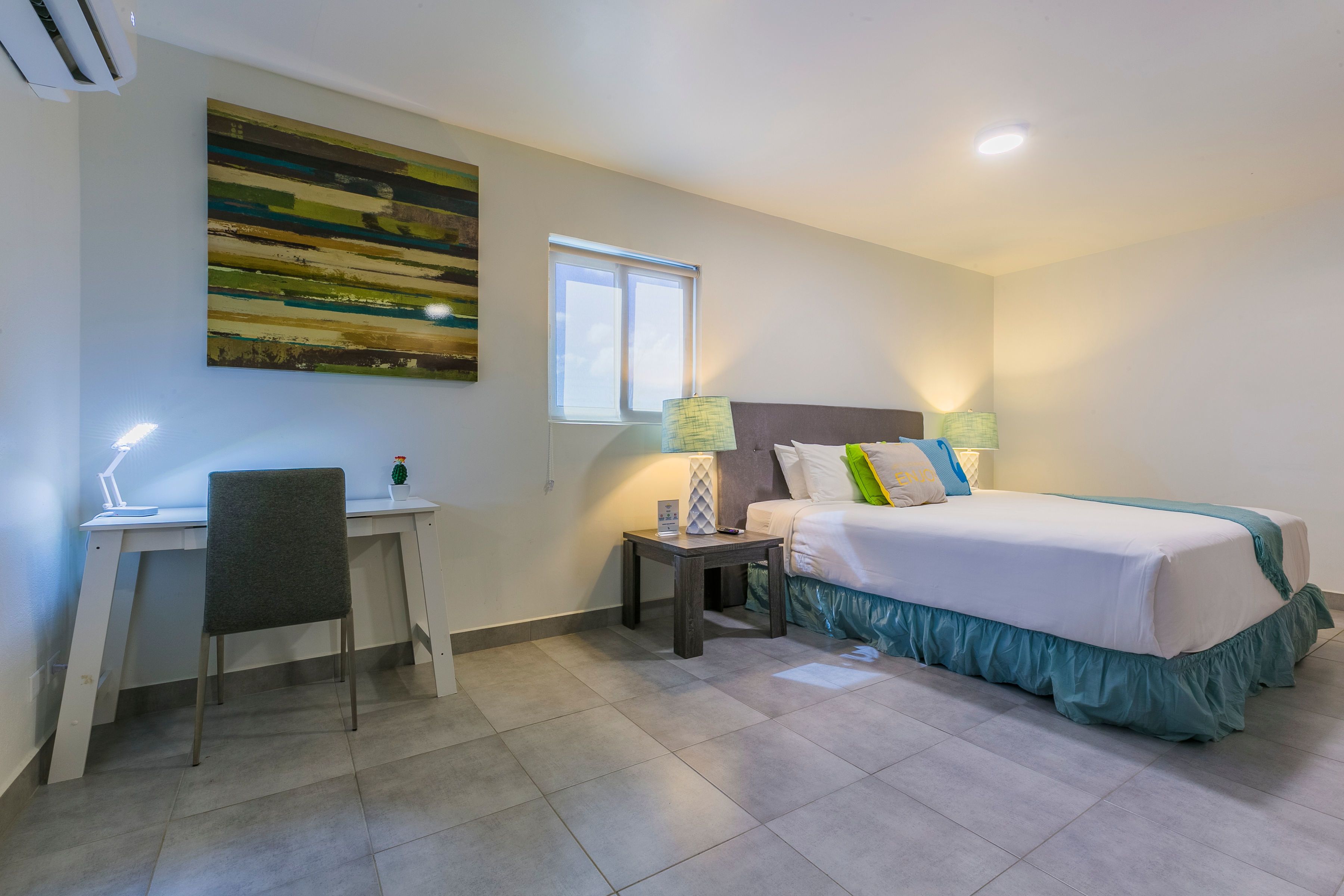 Quarto de hotel com cama, escrivaninha, cadeira e um quadro na parede.