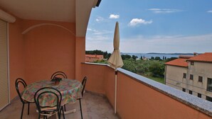Varanda com mesa e cadeiras, um guarda-sol e vista para a água e edifícios.