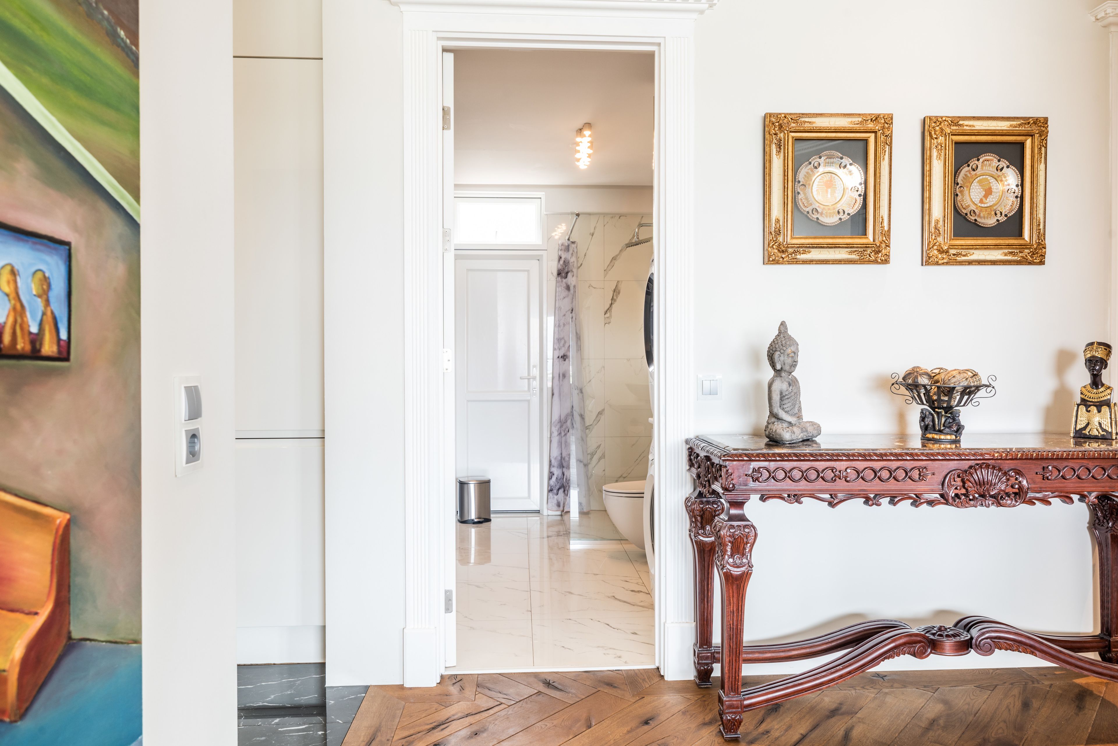 Um corredor com piso de mármore, um console de madeira com objetos decorativos e um quadro na parede.