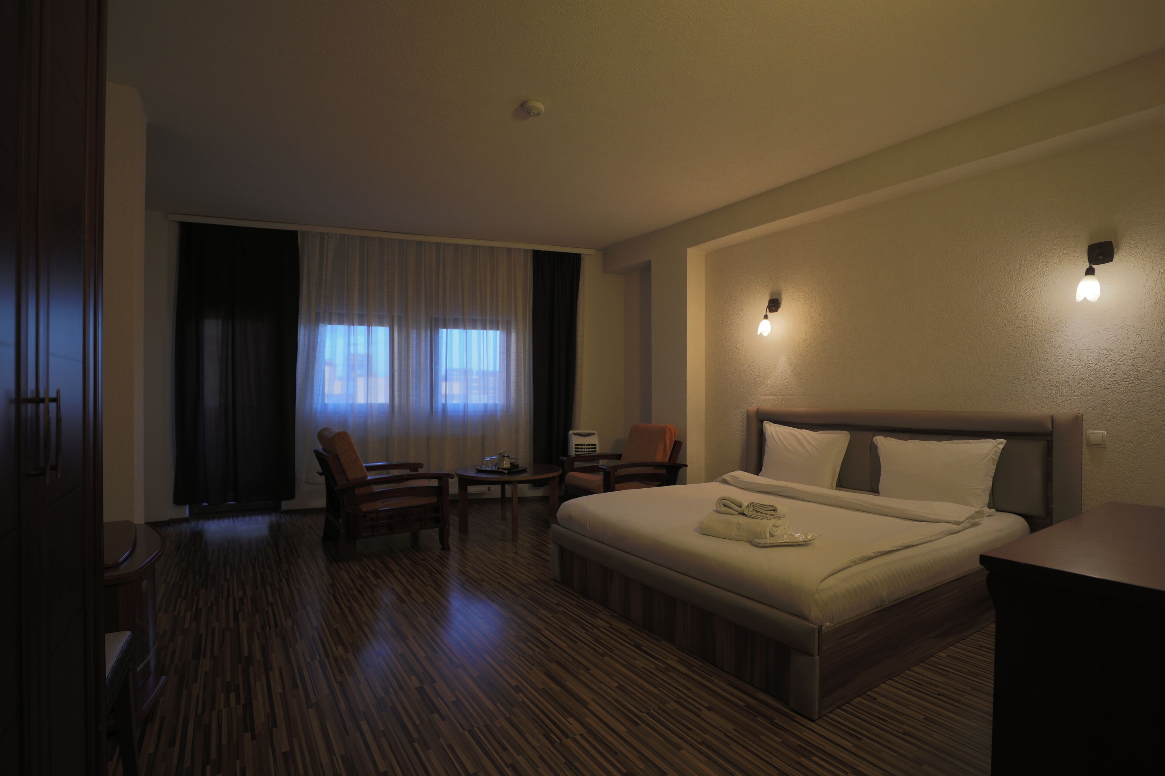 Quarto de hotel com cama, duas cadeiras, uma mesinha e uma escrivaninha.