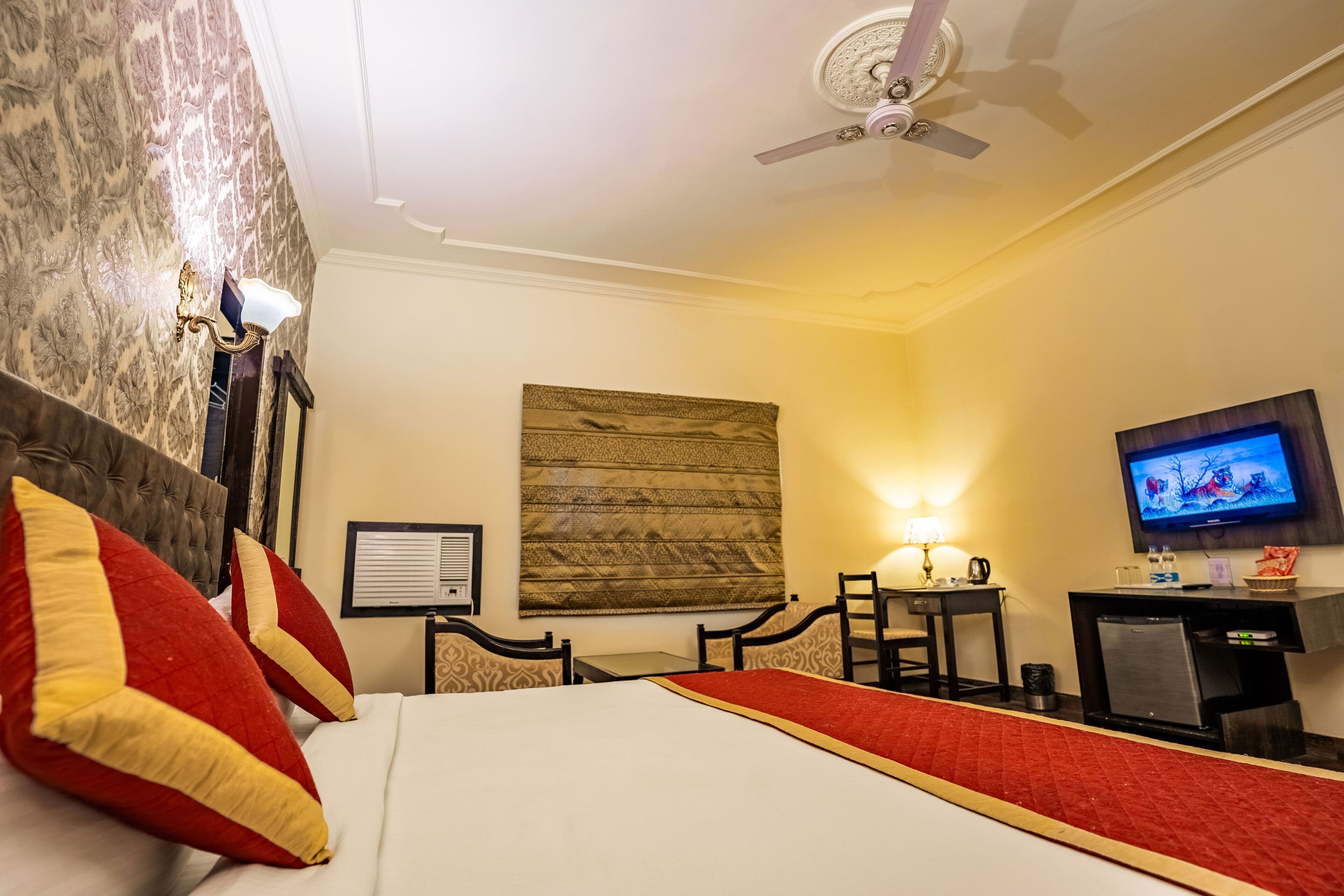 Quarto de hotel com cama, escrivaninha, televisão e ventoinha no teto.