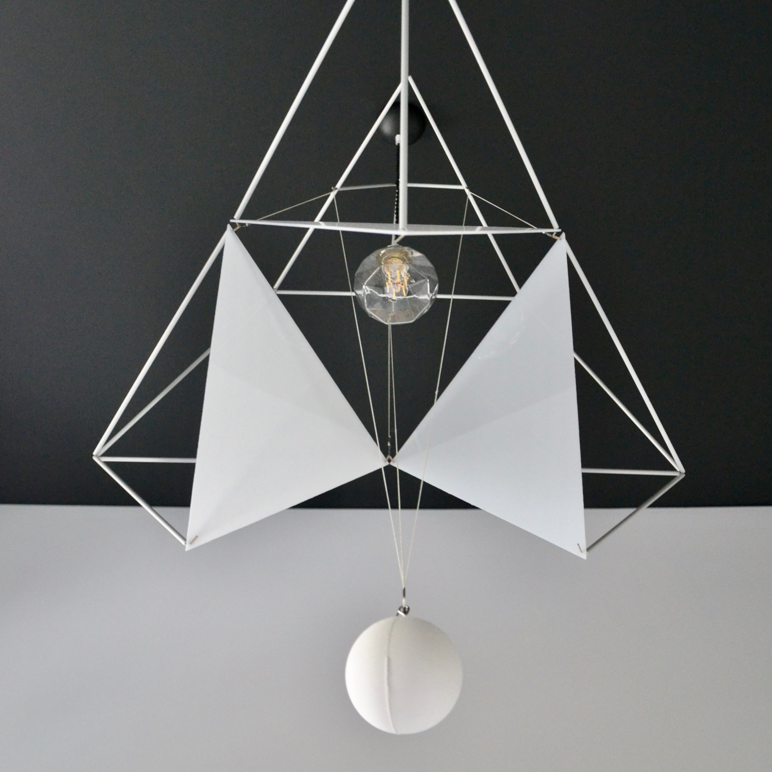 Um candelabro geométrico com uma luminária esférica e um objeto pendente esférico.