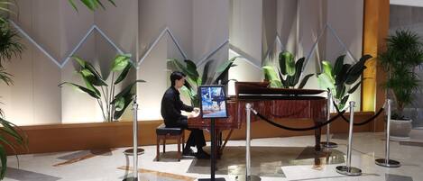 Um piano num hall com design moderno, cercado por plantas em vasos e uma barreira de vidro.