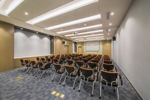 Uma sala de conferências com fileiras de cadeiras, uma tela de projetor e um ecrã de apresentação.