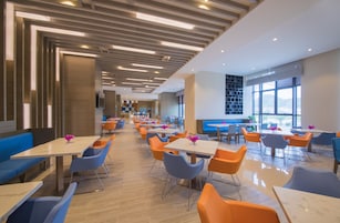 Uma sala de jantar moderna com várias mesas e cadeiras, piso de madeira e uma grande janela com vista para o exterior.