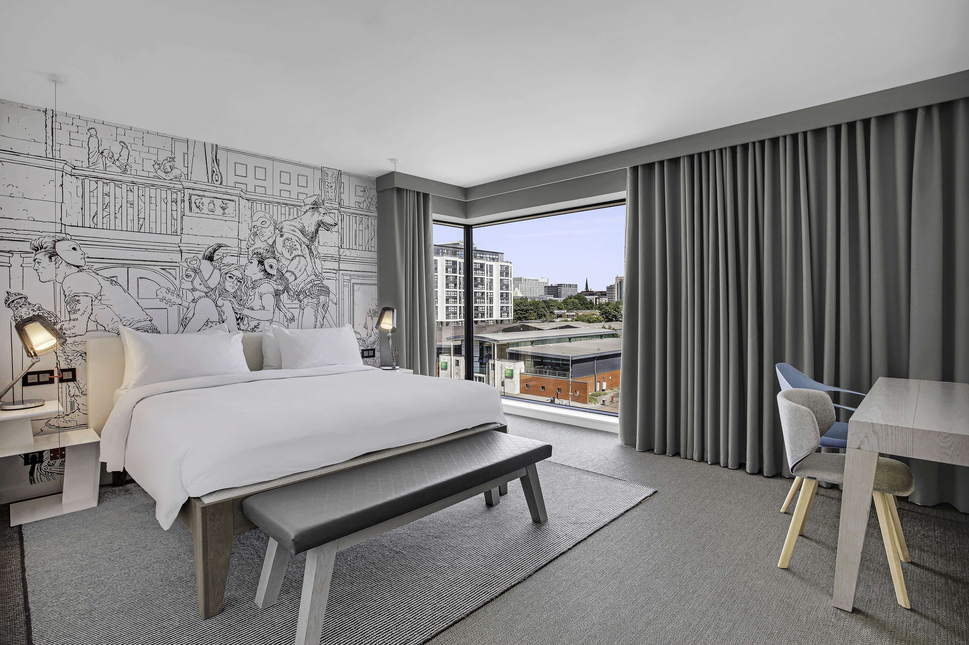 Quarto de hotel moderno com uma cama grande, uma escrivaninha e vista para a cidade.