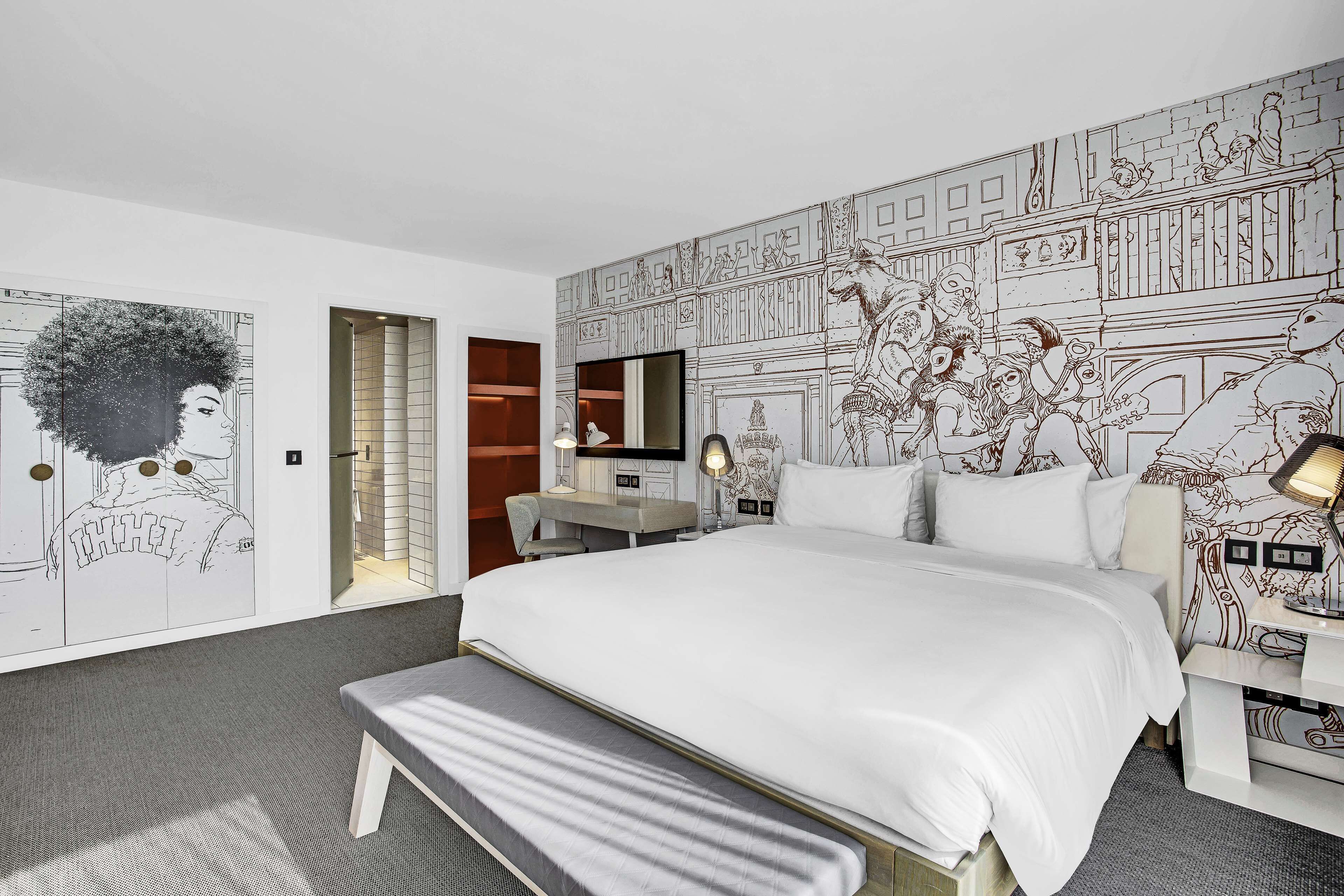 Quarto de hotel moderno com uma cama grande, uma escrivaninha, um espelho e papel de parede com tema egípcio.