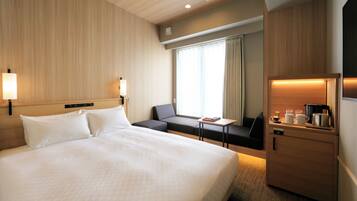 Quarto de hotel com uma cama grande, um sofá pequeno, uma escrivaninha e um mini-bar.