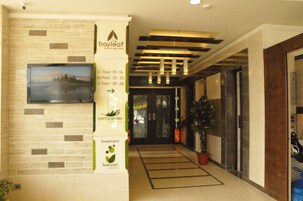 Um hall de hotel com parede de tijolos, uma televisão montada, placas de sinalização para os andares e um vaso de plantas.