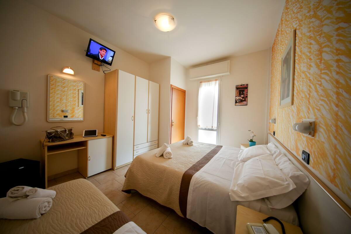 Quarto de hotel com duas camas, uma escrivaninha, uma televisão e banheiro.