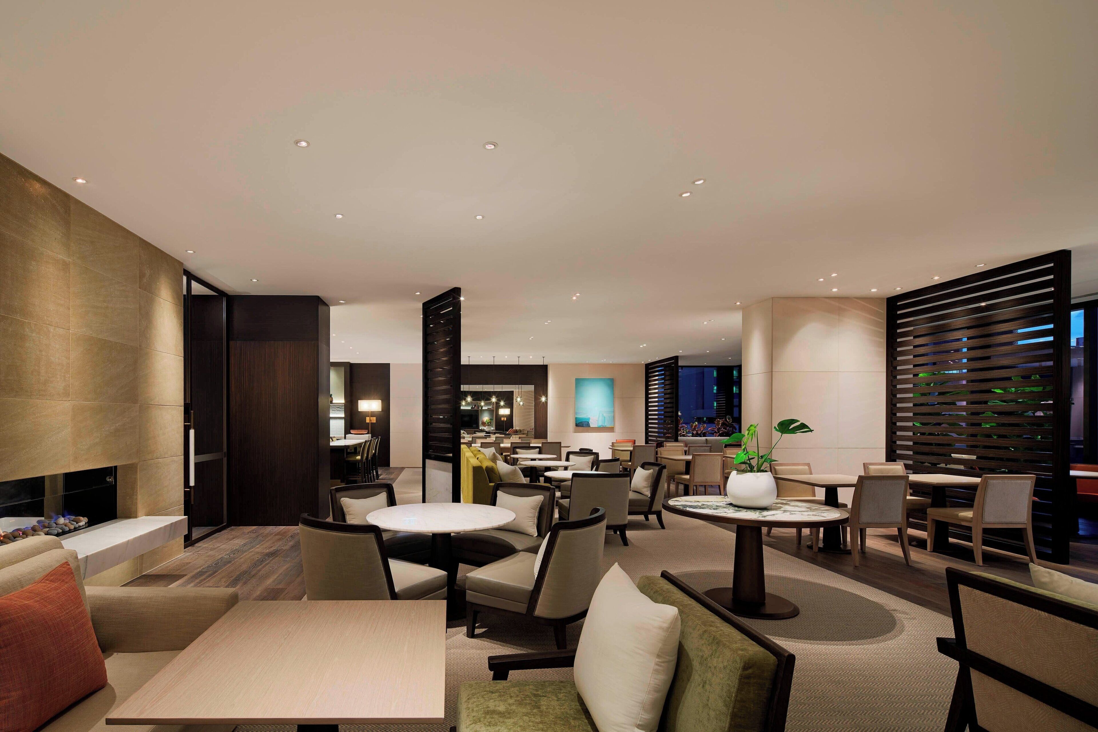 Um lobby moderno de hotel com várias áreas de estar, uma lareira e vista para a sala de jantar.