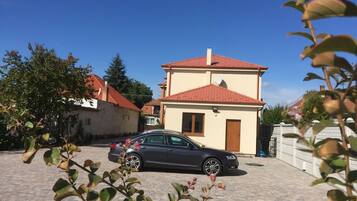 Um edifício de dois andares com telhado de telhas vermelhas, um carro estacionado na frente e um caminho de paralelepípedos.