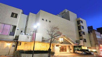Hotel com fachada moderna, entrada visível e área de estacionamento.
