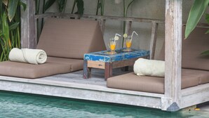 Uma área de descanso à beira da piscina, com duas cadeiras confortáveis, uma mesa com bebidas e uma toalha.