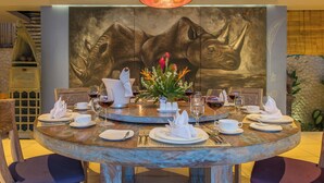 Mesa de jantar redonda posta para refeição, com uma grande pintura de rinocerontes ao fundo.