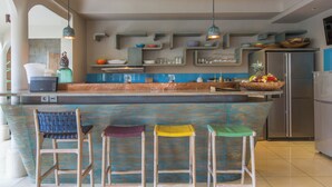 Uma cozinha com uma ilha central, banquetas e uma geladeira.