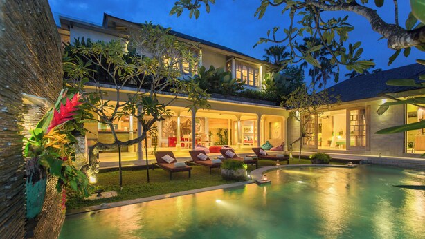 Uma área de piscina luxuosa, com espreguiçadeiras e um edifício bem iluminado ao fundo.