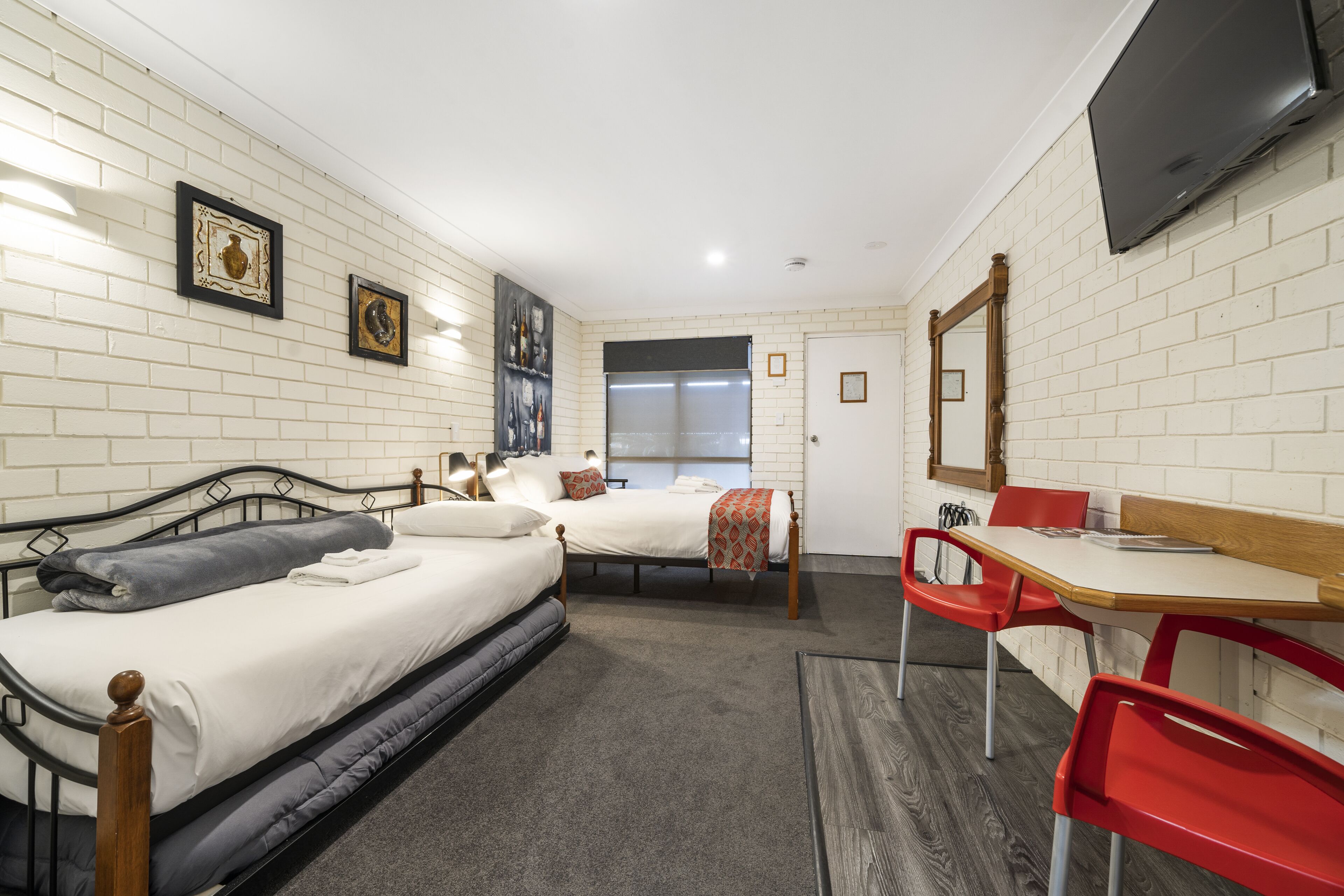 Quarto de hotel com duas camas, uma escrivaninha, uma cadeira, televisão e obras de arte nas paredes.