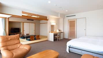 Quarto de hotel com cama, escrivaninha, cadeira, sofá e televisão.