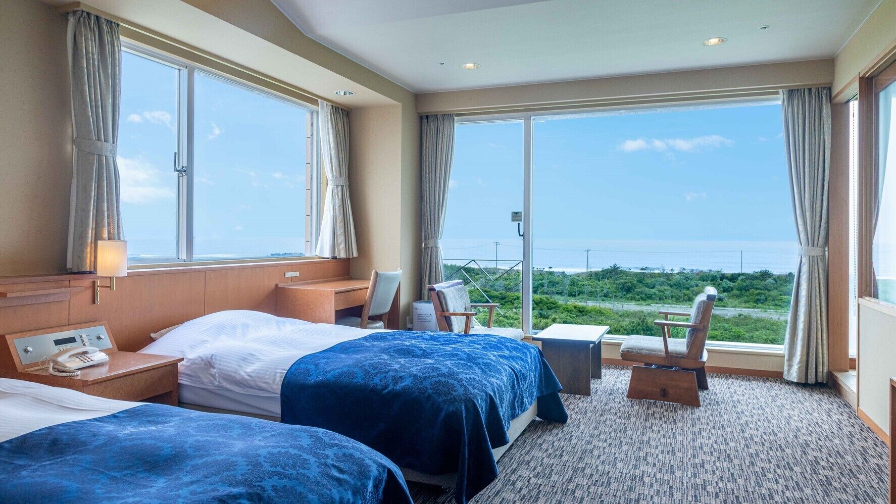 Quarto de hotel com duas camas, uma mesa, uma cadeira e vista para o oceano.