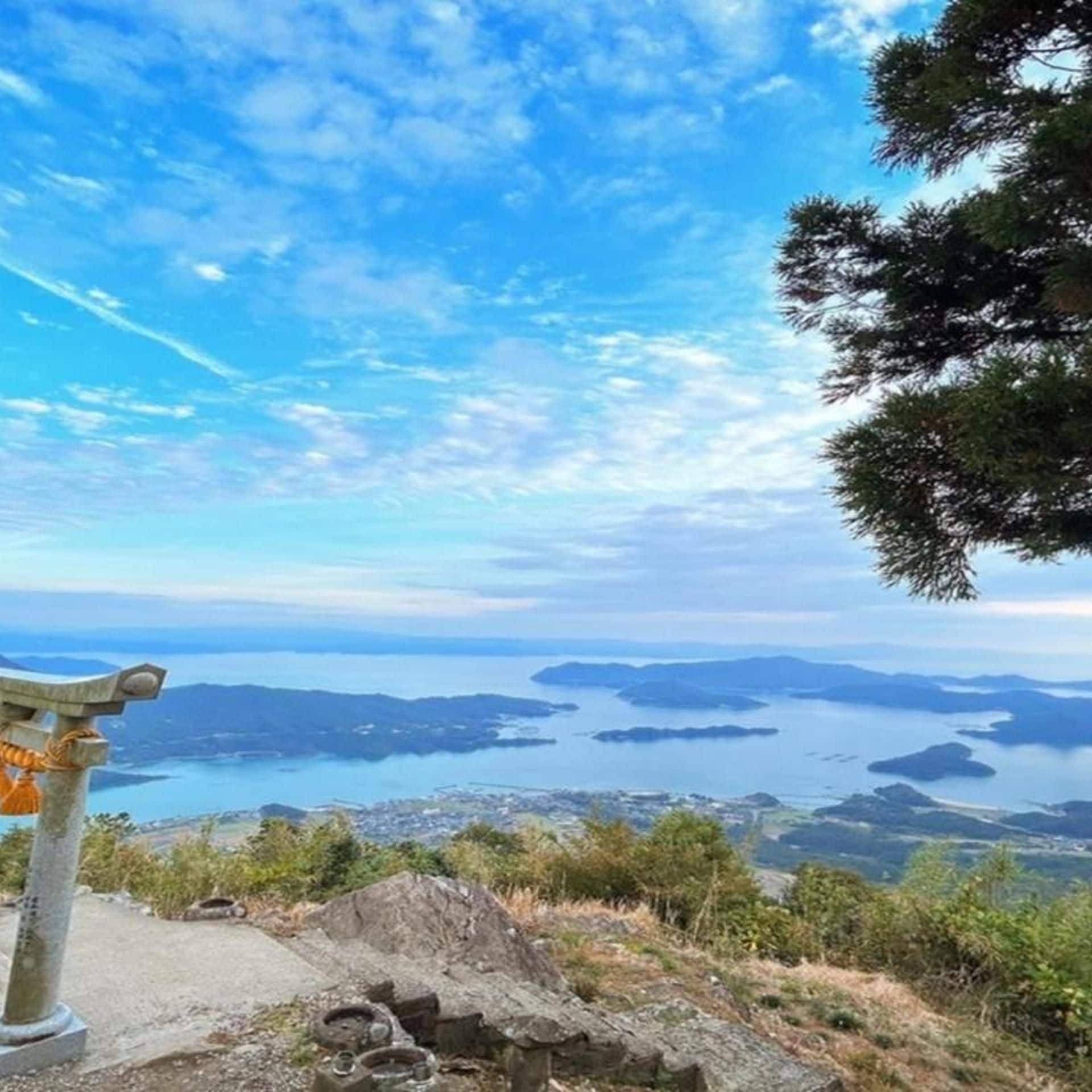 Paisagem costeira com céu claro, estrutura de pedra e vista para o mar e ilhas.