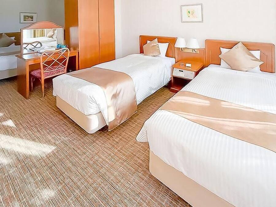 Quarto de hotel com duas camas, uma escrivaninha e uma cadeira.