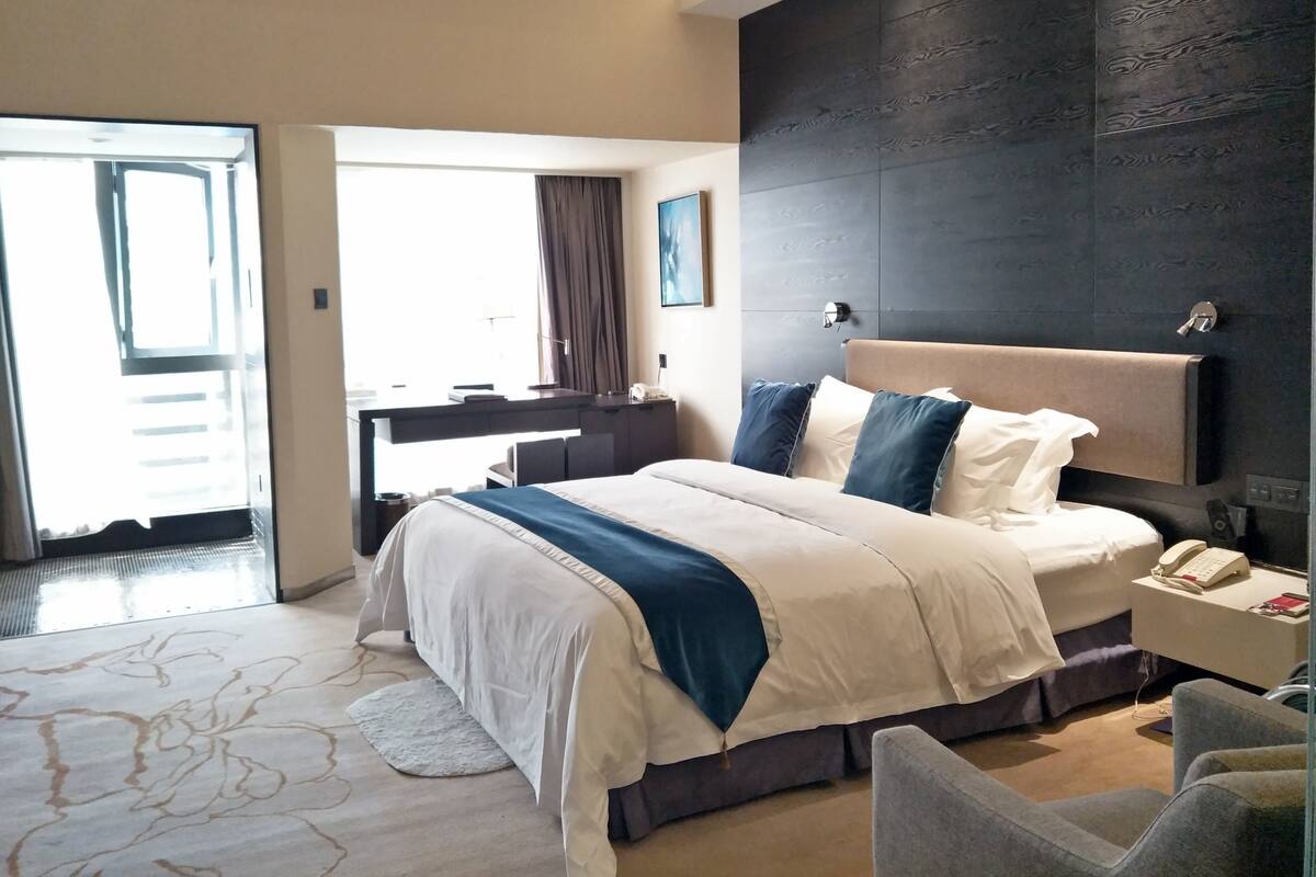Quarto de hotel moderno com uma cama grande, mesa de cabeceira e escrivaninha com cadeira.
