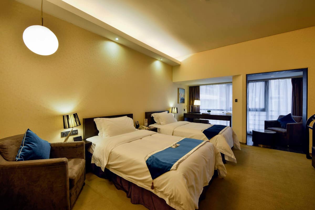 Quarto de hotel com duas camas, um sofá, uma escrivaninha e uma cadeira.