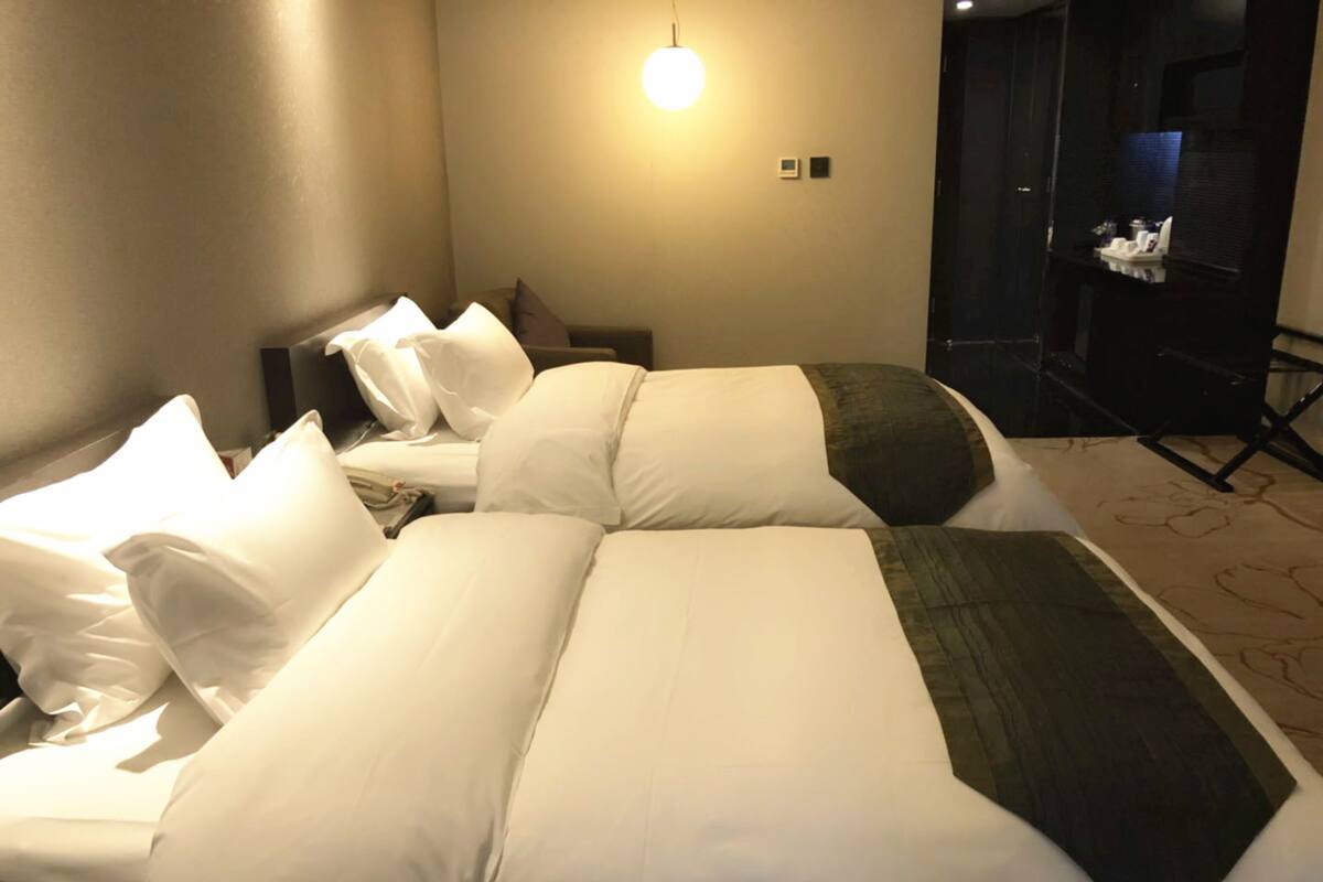 Quarto de hotel com duas camas, uma escrivaninha e um guarda-roupa.