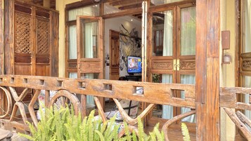 Um portão de madeira tradicional com intrincados entalhes, dando acesso a um quarto com televisão e decoração na parede.