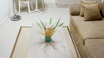 Uma sala de estar moderna com uma mesa de centro de madeira, um sofá, uma área de jantar com cadeiras e uma cozinha ao fundo.
