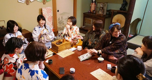 Um grupo de pessoas sentadas em torno de uma mesa de madeira em um ambiente com decoração tradicional, incluindo um painel shoji e um pequeno santuário.