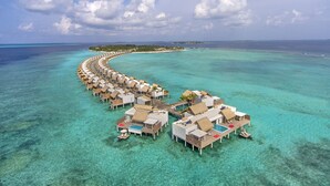 Um resort sobre a água com diversas acomodações tipo bangalô interligadas por uma passarela.