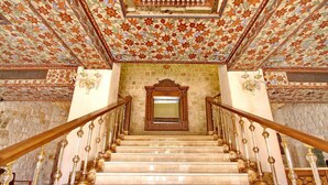 Uma escadaria imponente com grades ricamente decoradas e teto ornamental.