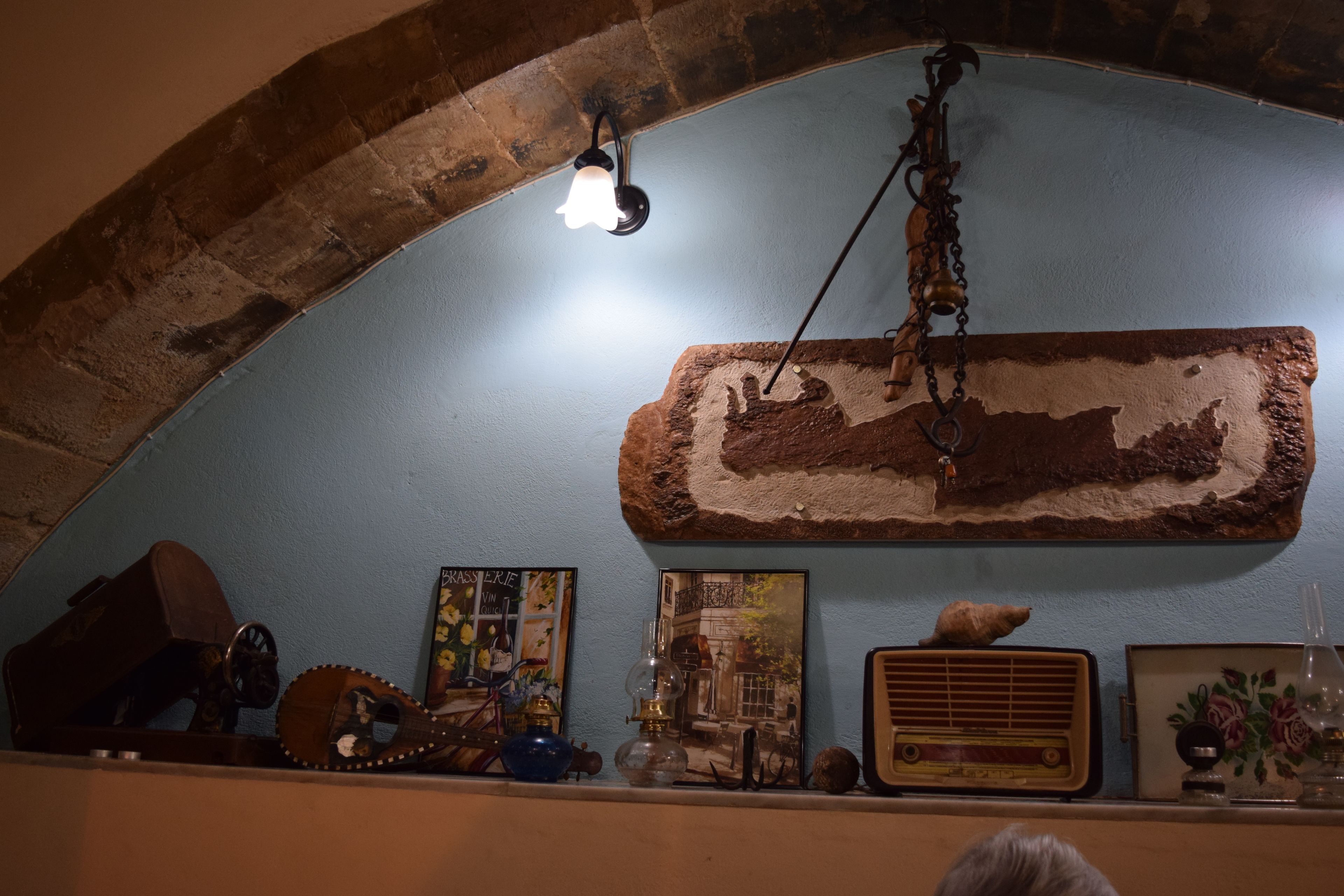 Um quarto com um arco de pedra, um baú de madeira, um rádio antigo e diversas molduras com fotos na parede.