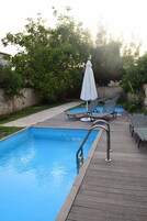 Um deck de madeira com piscina, espreguiçadeiras e um guarda-sol.