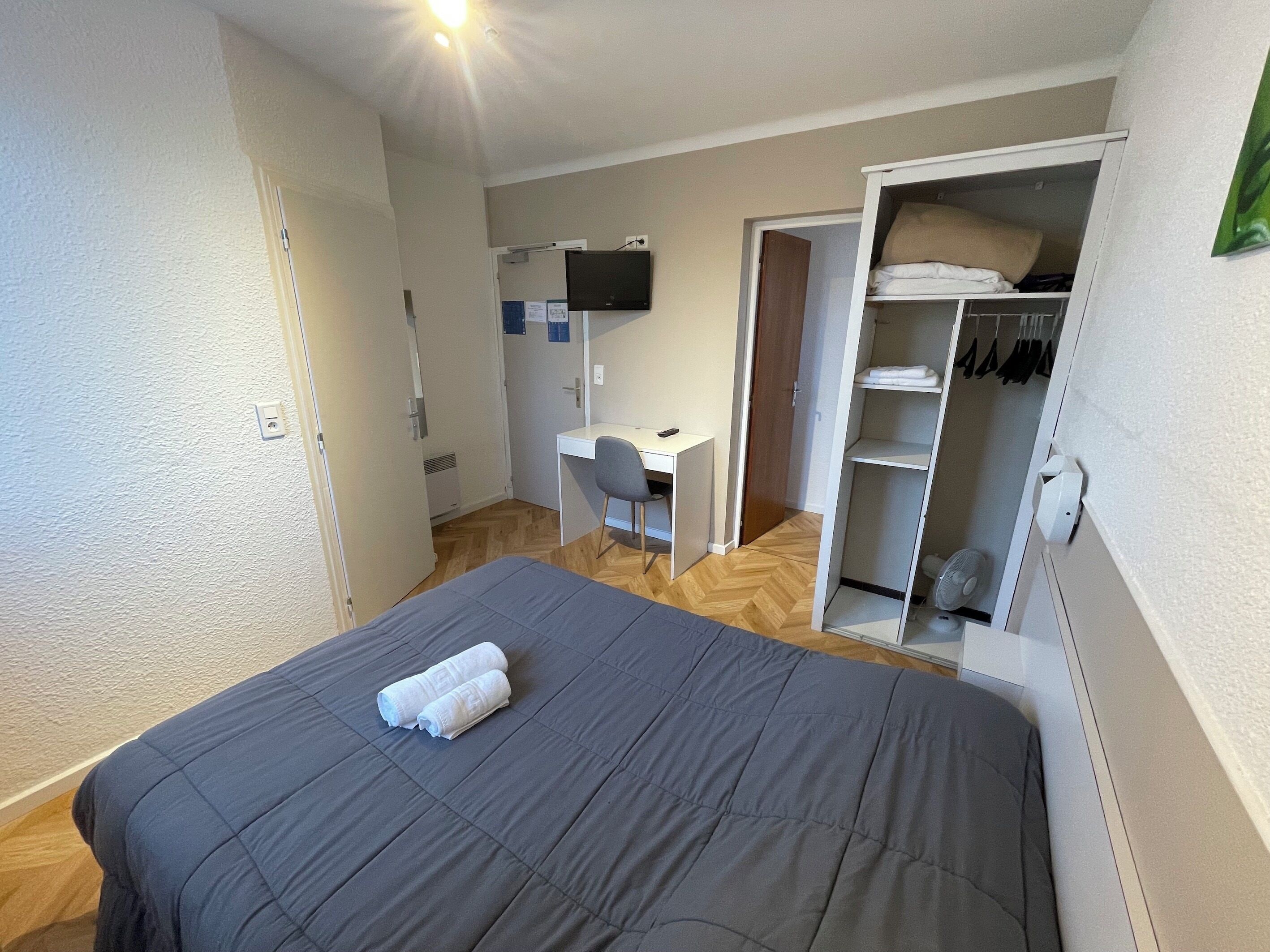 Quarto de hotel com cama, secretária, cadeira, televisão e guarda-roupa.