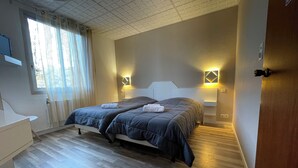 Quarto com cama de casal, duas mesas de cabeceira com luminárias, janela com cortinas e piso de madeira.