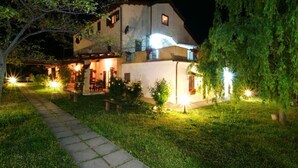 Uma casa de dois andares com um caminho de pedras que leva à entrada, cercada por vegetação e iluminada por luzes externas.