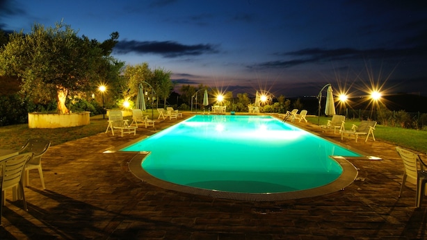 Piscina retangular com espreguiçadeiras e guarda-sóis, ladeada por um deck revestido de azulejos.