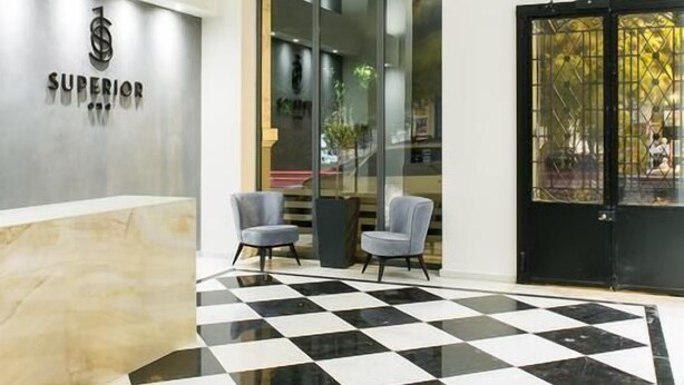 Um hall com piso xadrez, balcão de recepção e uma escadaria.