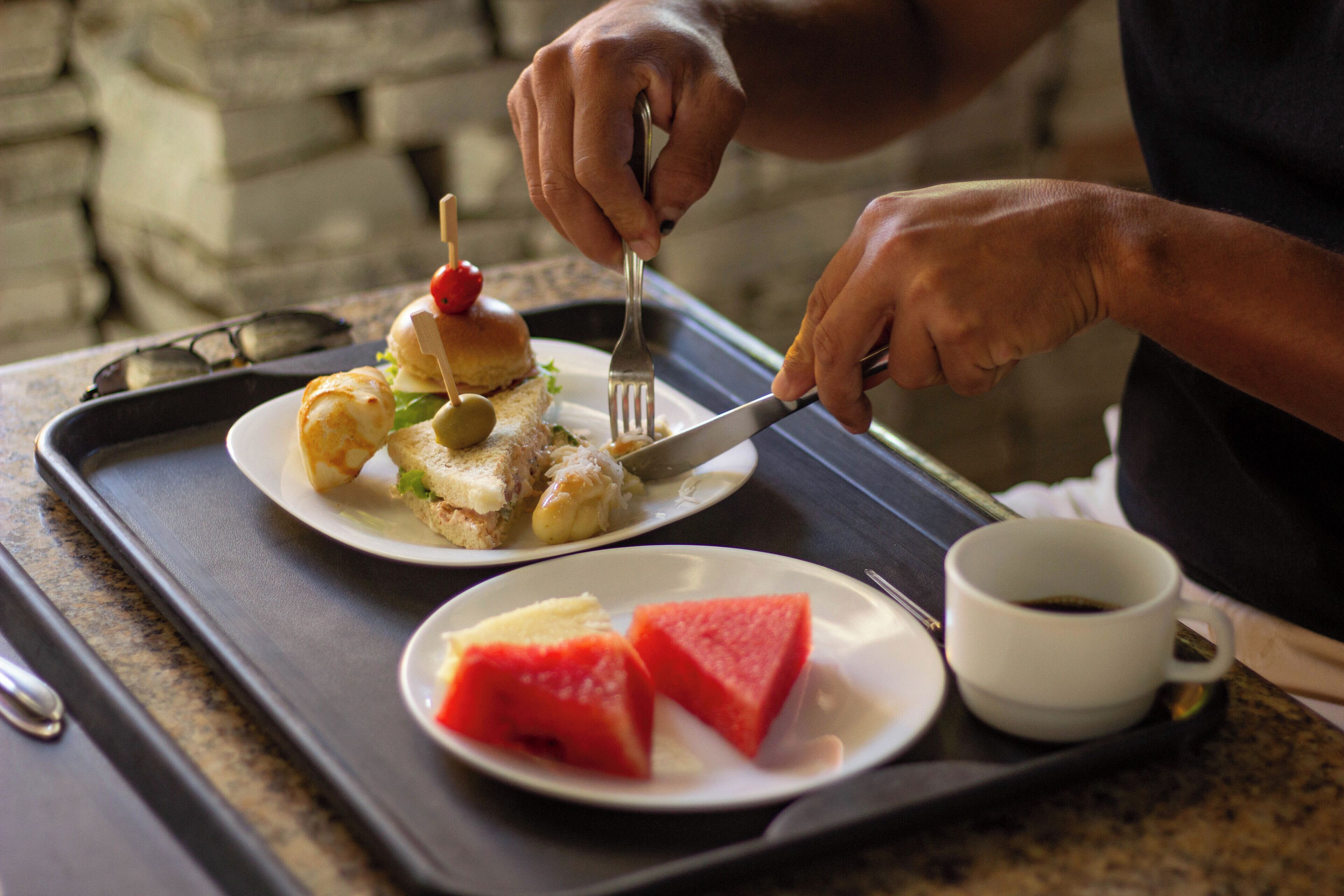 Uma bandeja com sanduíche, uma fatia de melancia e uma xícara de café.