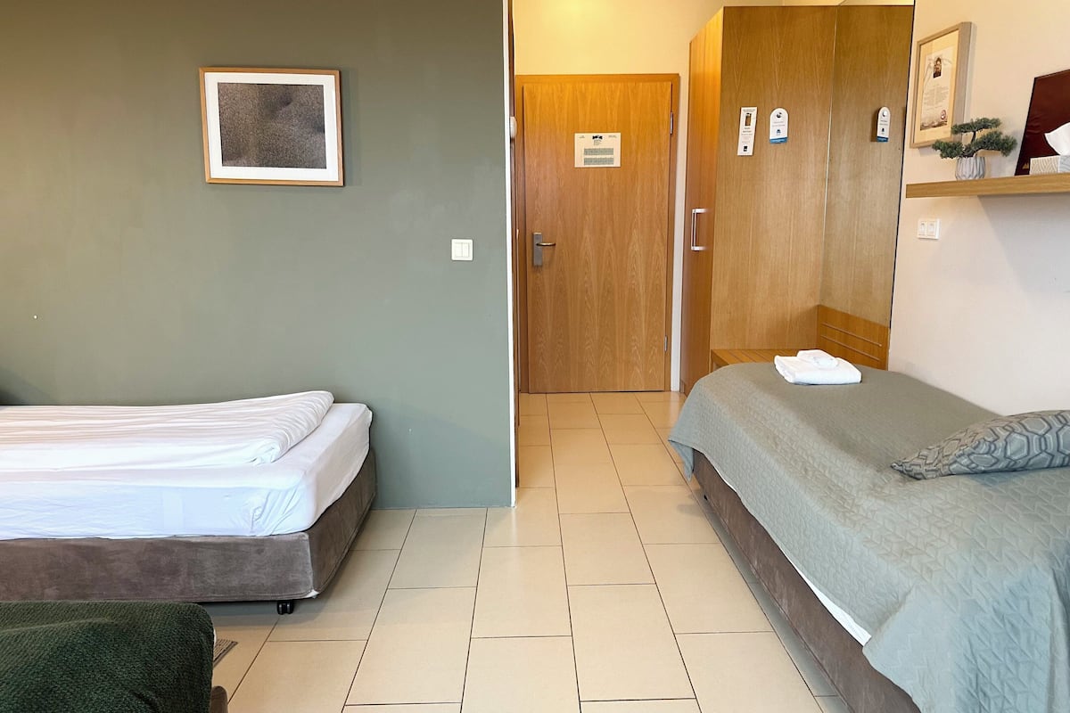 Quarto de hotel com duas camas, um guarda-roupa de madeira, um quadro na parede e uma pequena mesa com uma toalha.