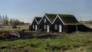 Uma fileira de três casas de madeira preta com detalhes em branco e telhados de grama.