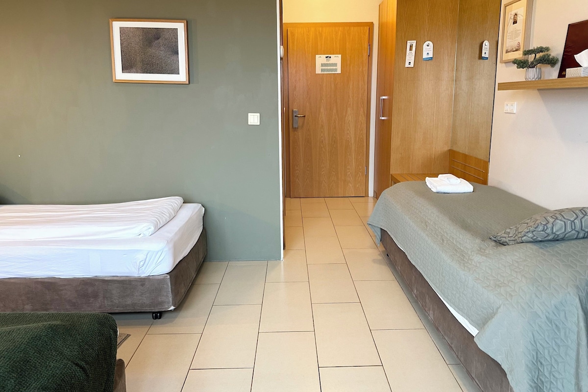 Quarto de hotel com duas camas, um guarda-roupa de madeira, um quadro na parede e uma pequena mesa com uma toalha.