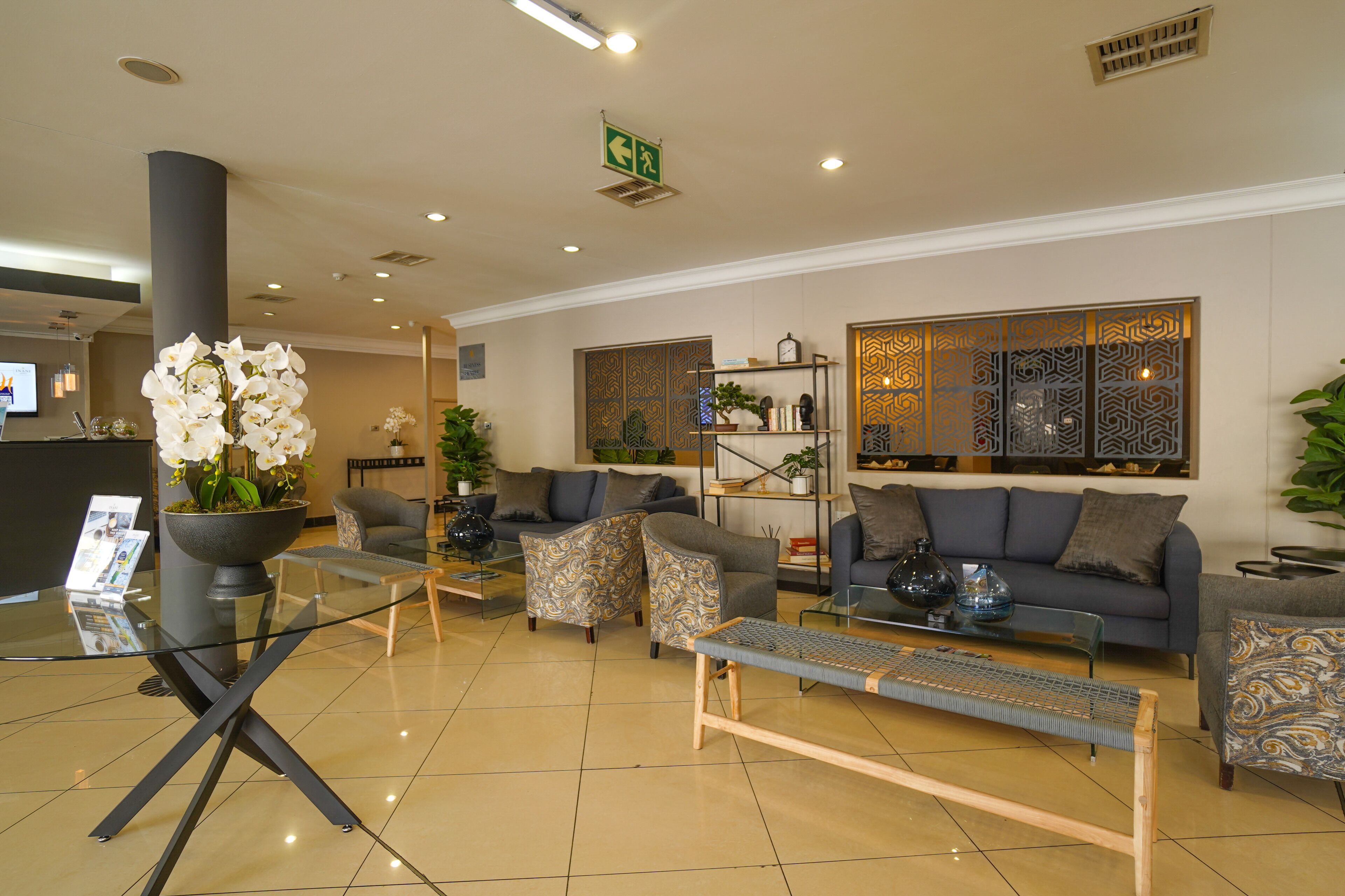 Um lobby moderno com uma recepção, área de estar e elementos decorativos como plantas e obras de arte.