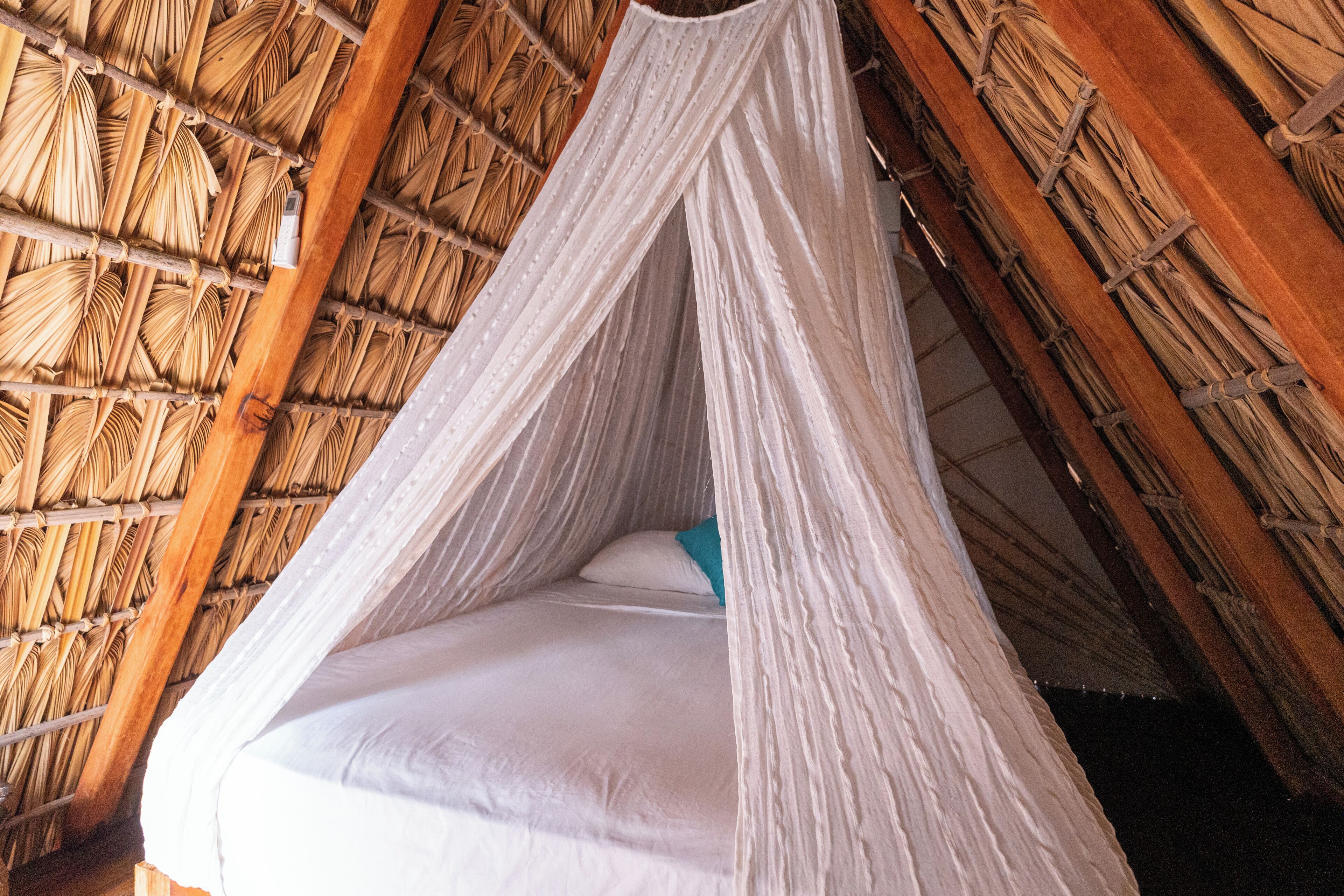 Uma cama com dossel branco em um quarto com telhado de palha.