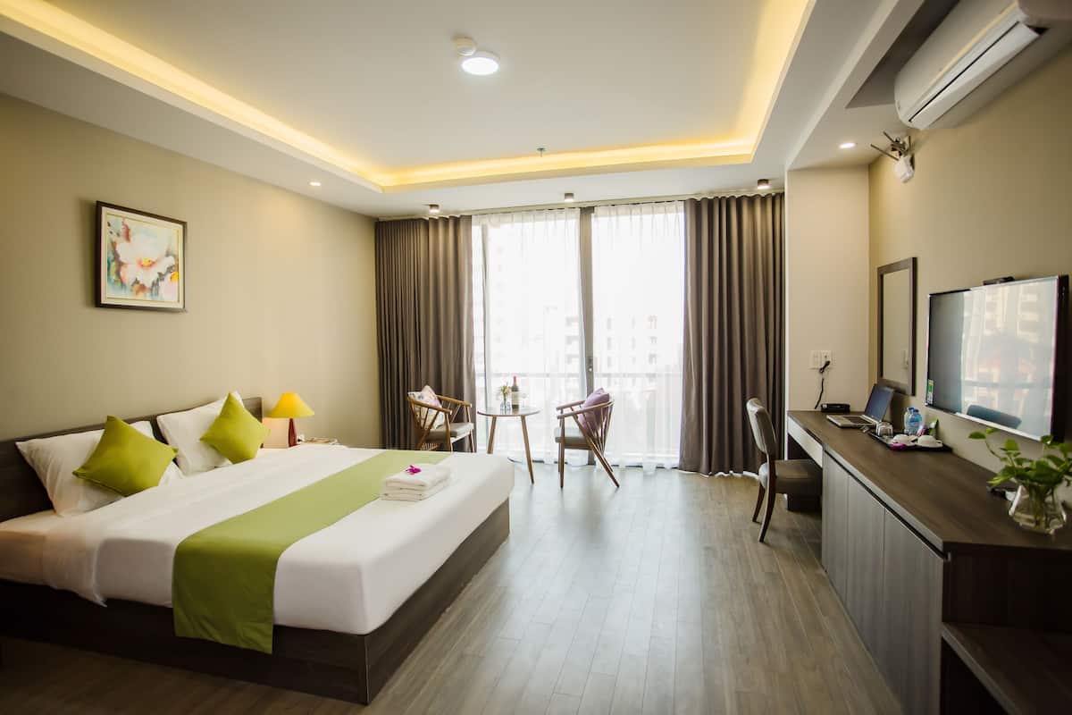 Quarto de hotel com cama, escrivaninha, cadeiras e televisão.