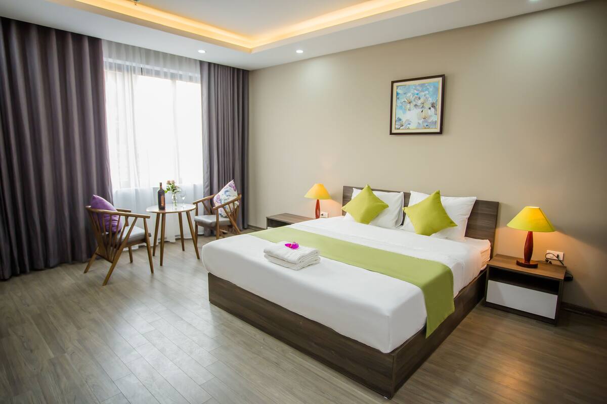 Quarto de hotel com uma cama grande, duas mesas de cabeceira, uma escrivaninha e uma cadeira.