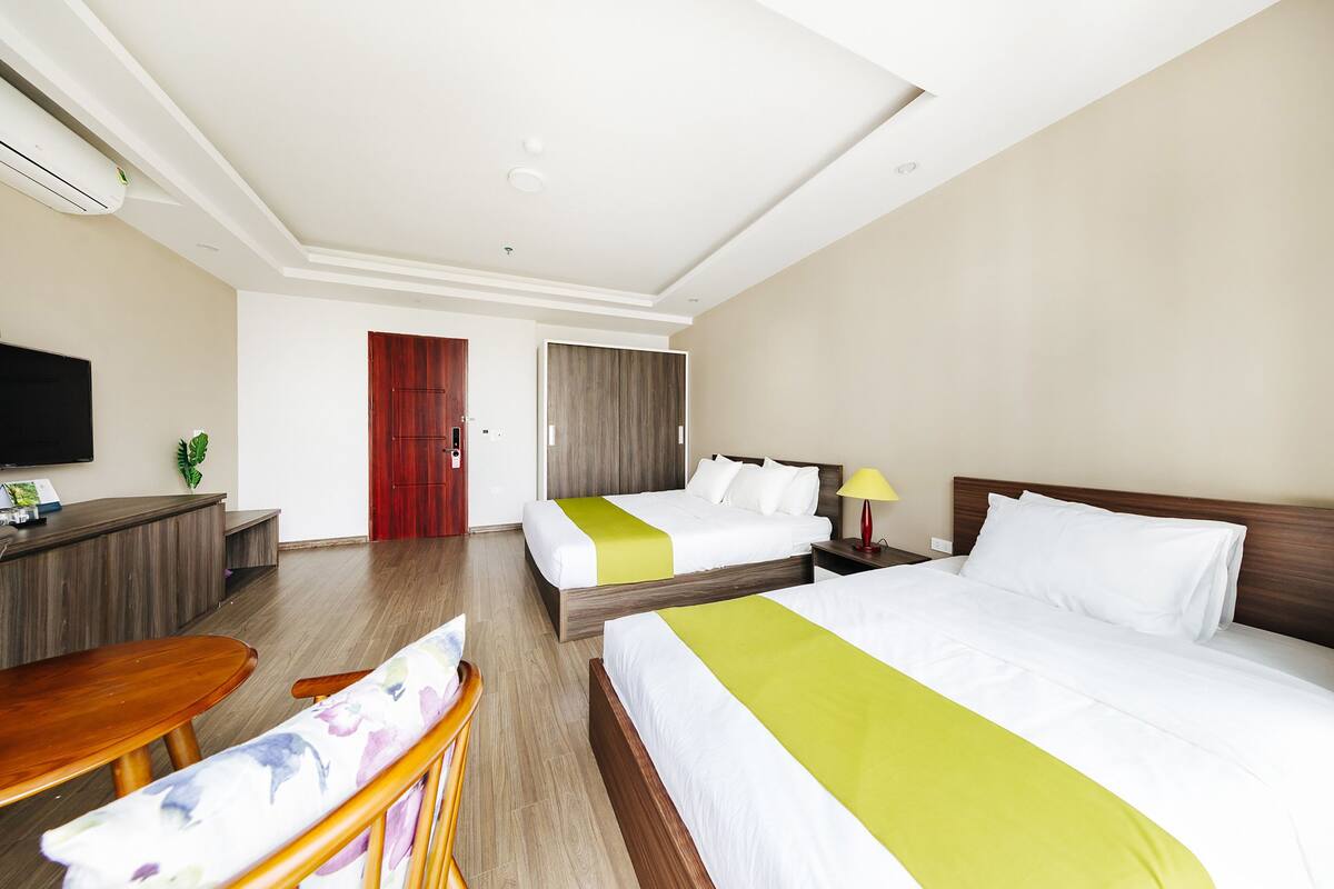 Quarto de hotel com duas camas, uma escrivaninha, uma cadeira e uma televisão.